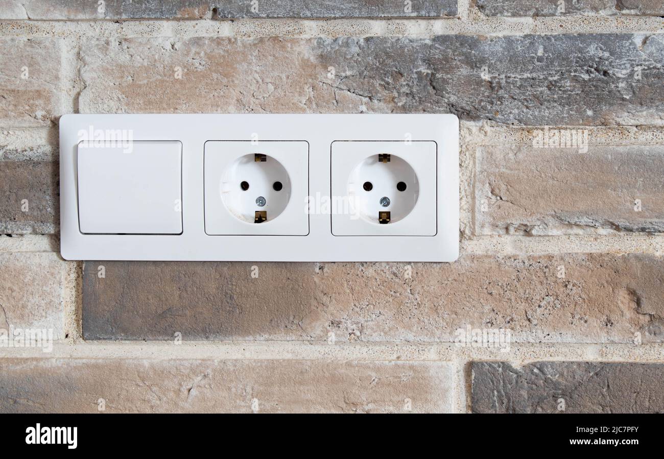 close up white electrical socket and white light switch on bricks wall ...