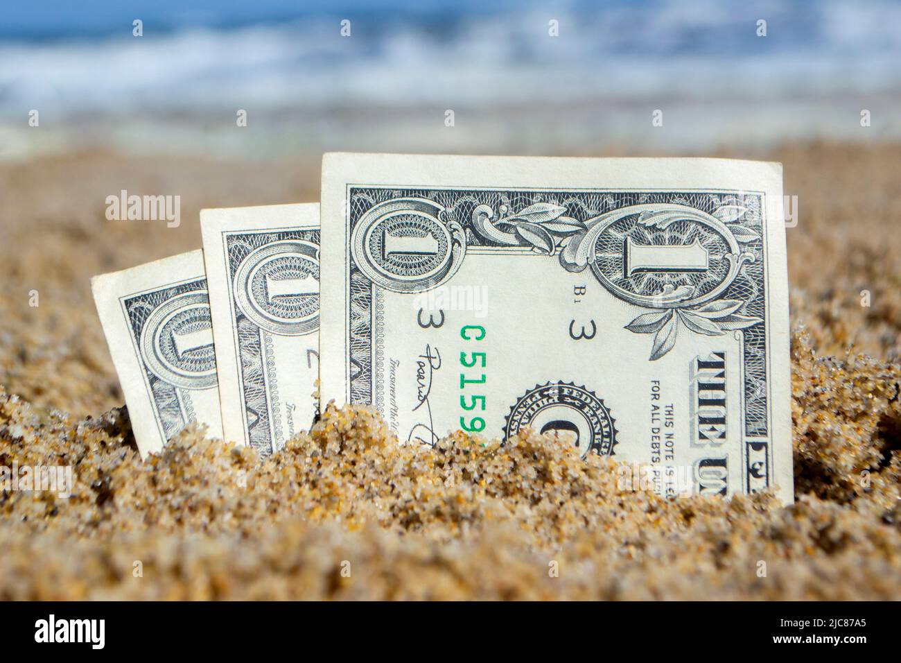 Paper bills one dollar buried in the sand on the beach against backdrop ...