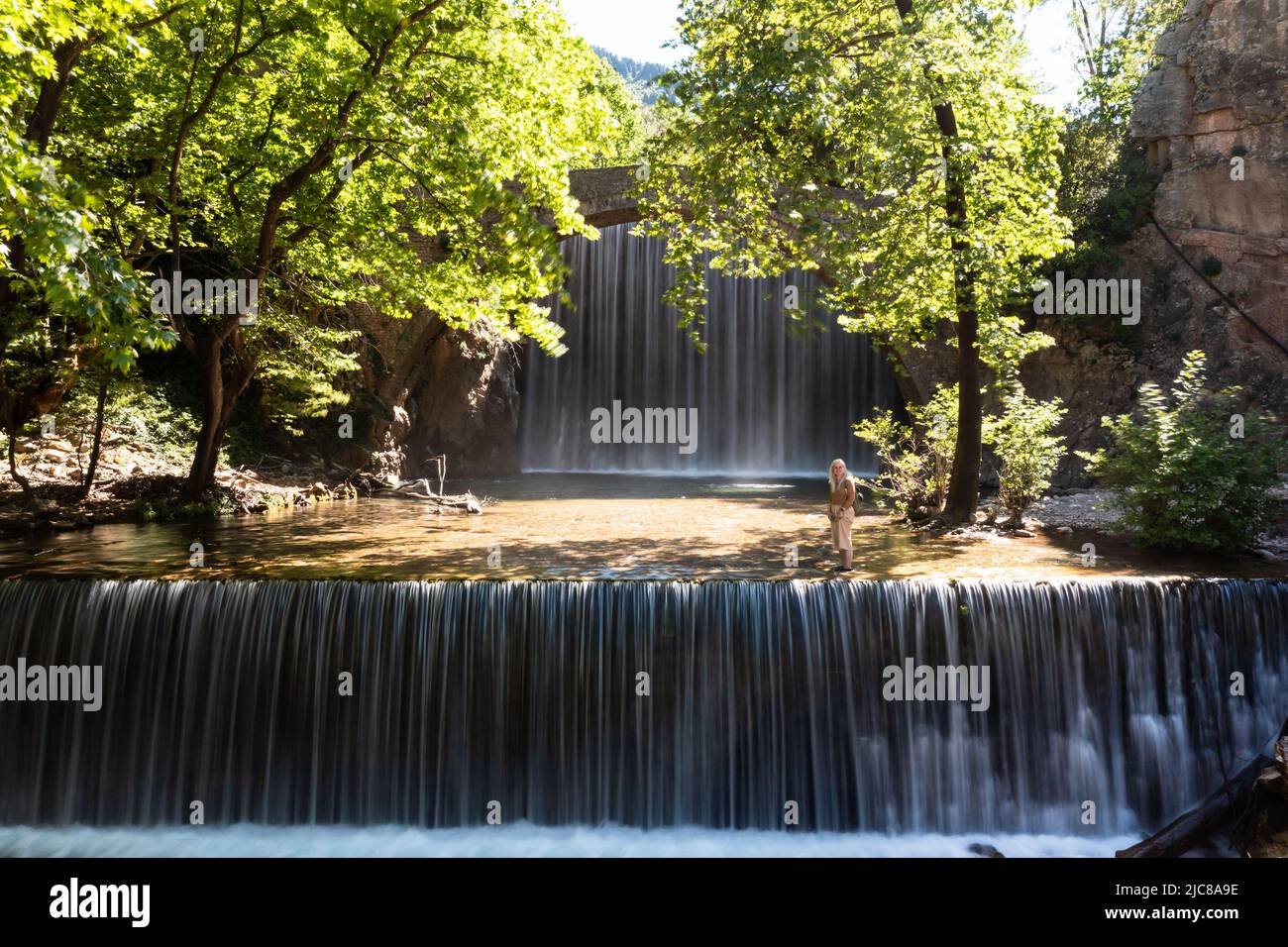 Blonde woman standing at the waterfalls at Palaiokarya Stone Arch ...