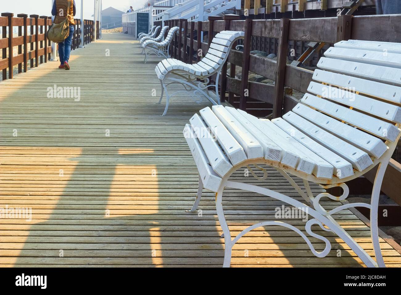 Row of white benches on a wooden boardwalk. Walking woman with a travel ...