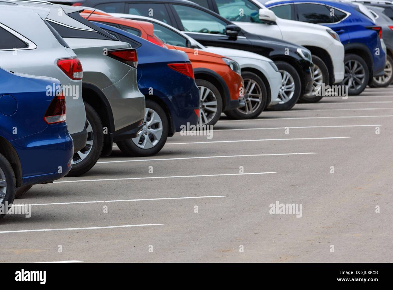 row of different color cars on asphalt parking lot at cloudy summer day ...