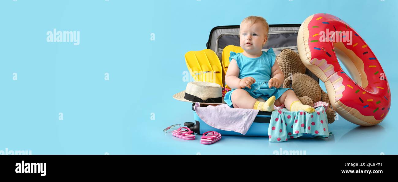 Adorable baby girl sitting in big suitcase with belongings on blue ...
