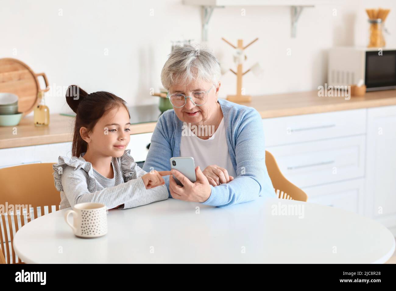Little girl with her grandma using mobile phone in kitchen Stock Photo ...