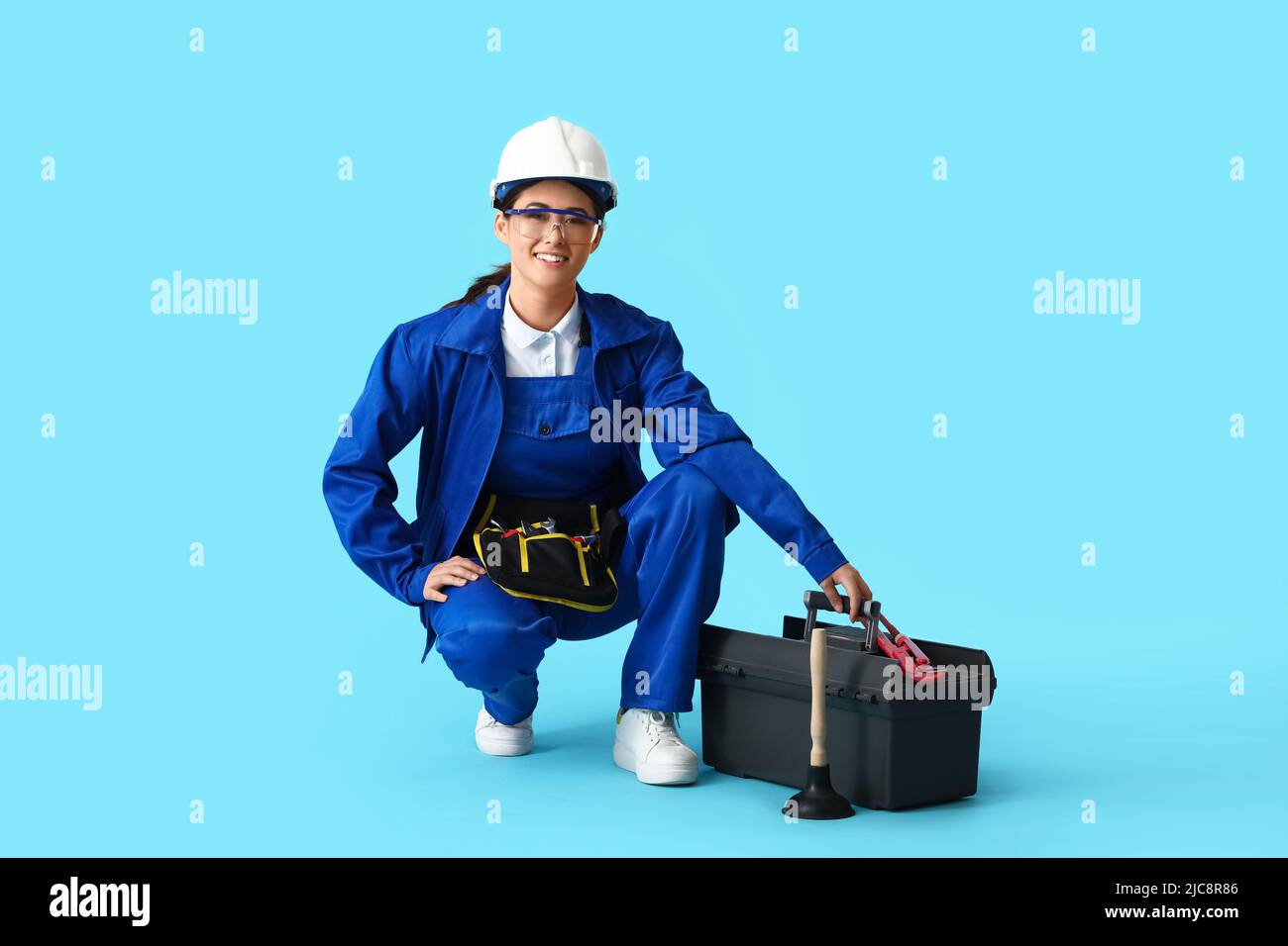Asian female plumber with bags on blue background Stock Photo - Alamy