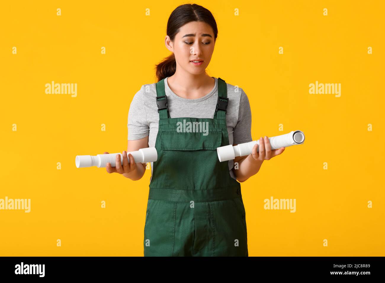 Asian female plumber with flexible hoses on yellow background Stock ...