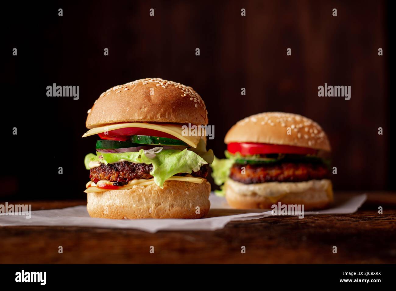 Two hamburgers on a wooden background. Big and small cheeseburger ...