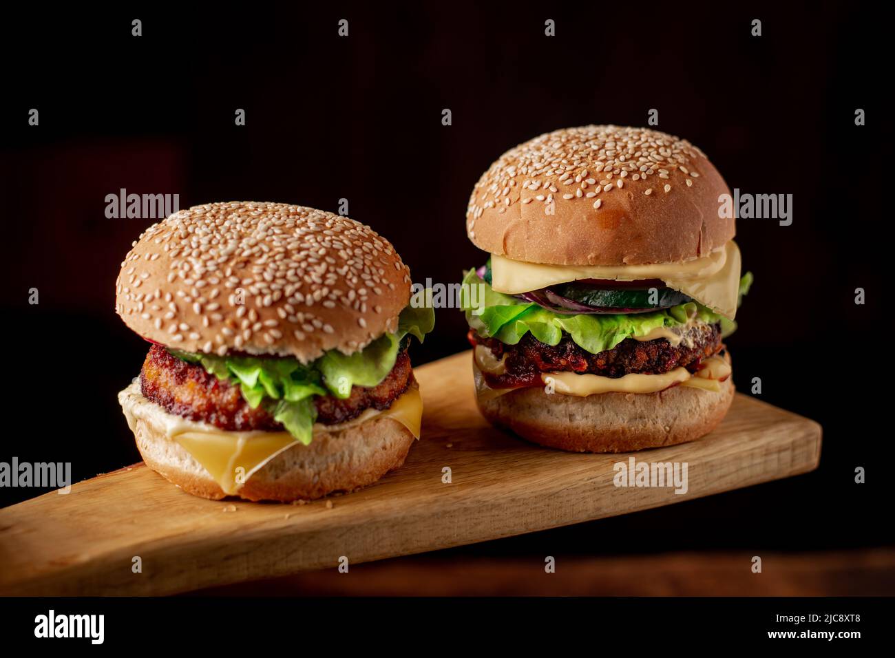 Two hamburgers on a wooden background. Big and small cheeseburger ...