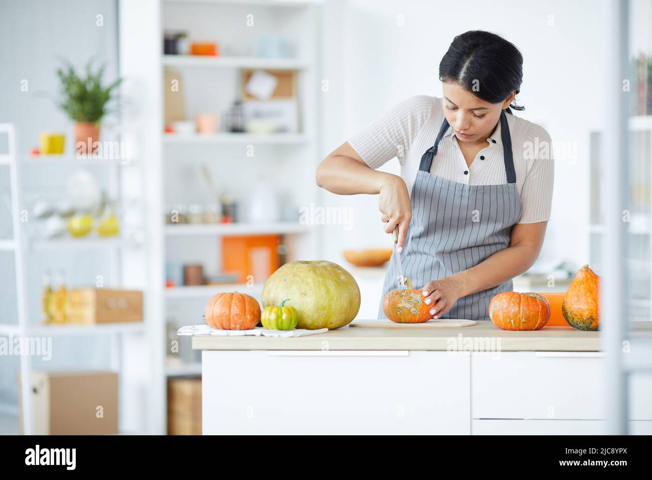 Description: Concentrated young black woman in stripped apron cutting ...