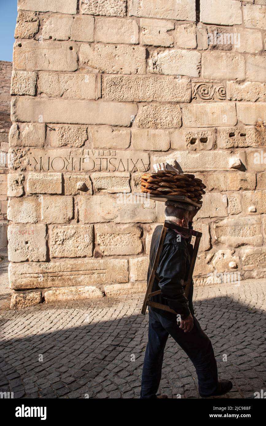 Simit seller walking past old city walls with Roman numerals carved in ...