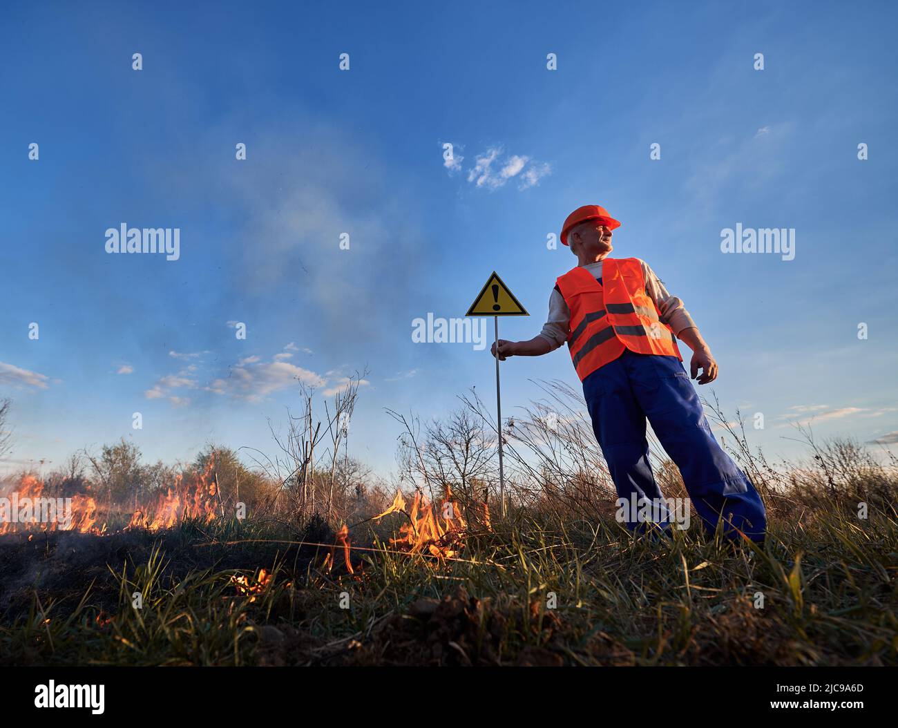 Firefighter ecologist fighting fire in field in evening. Man in orange ...