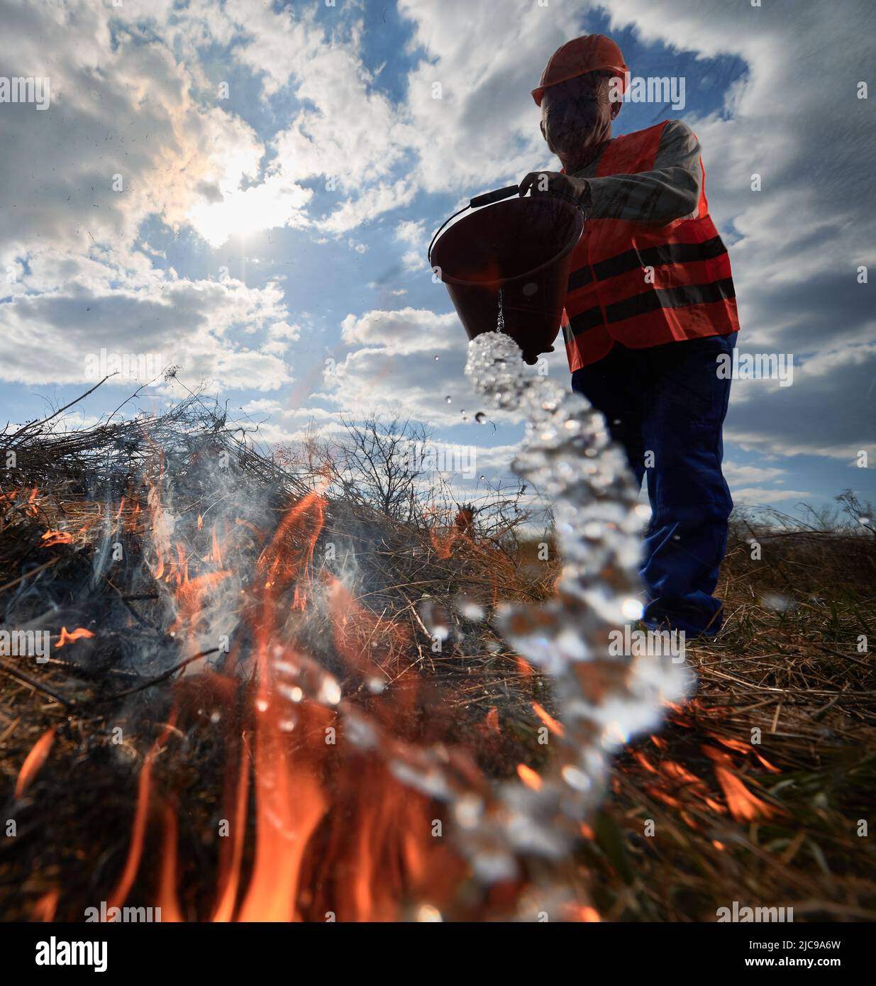 Fireman ecologist extinguishing fire in field with cloudy sky on ...