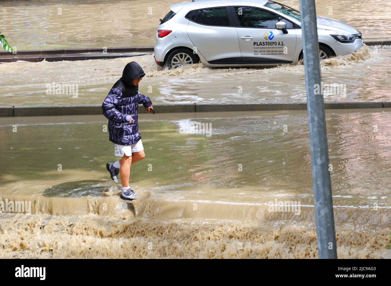 Young man trying to walk in flooded road with cars at back ground ...