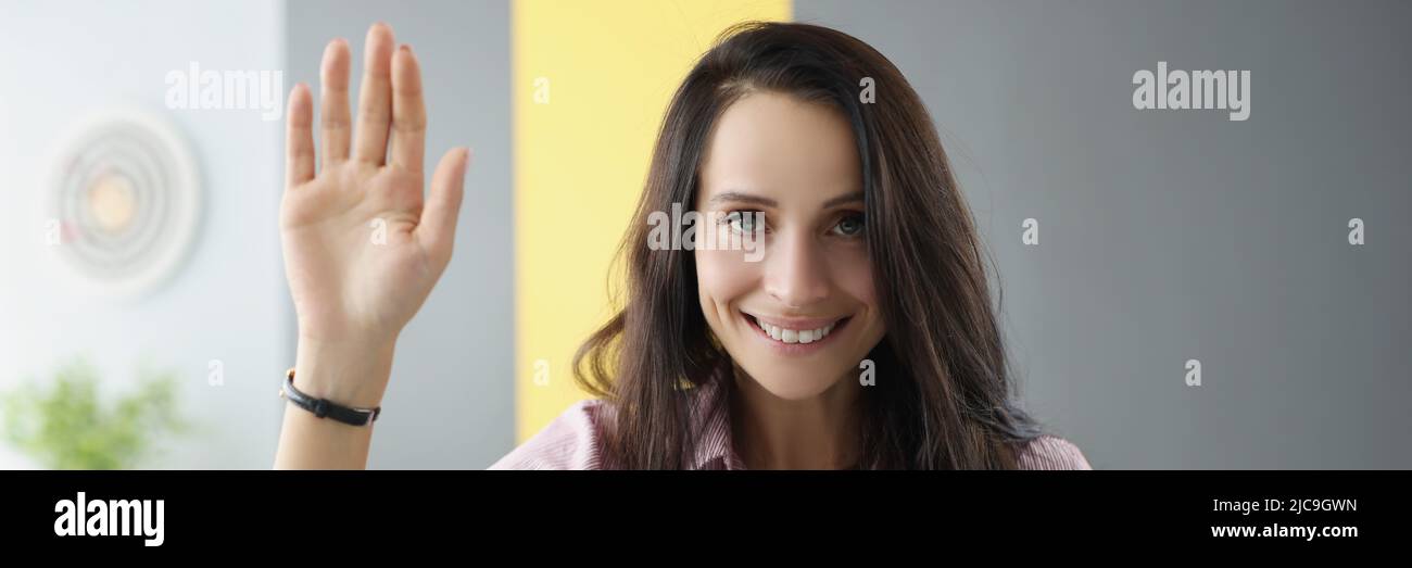 Beautiful young woman lift hand as hello gesture sit in living room ...