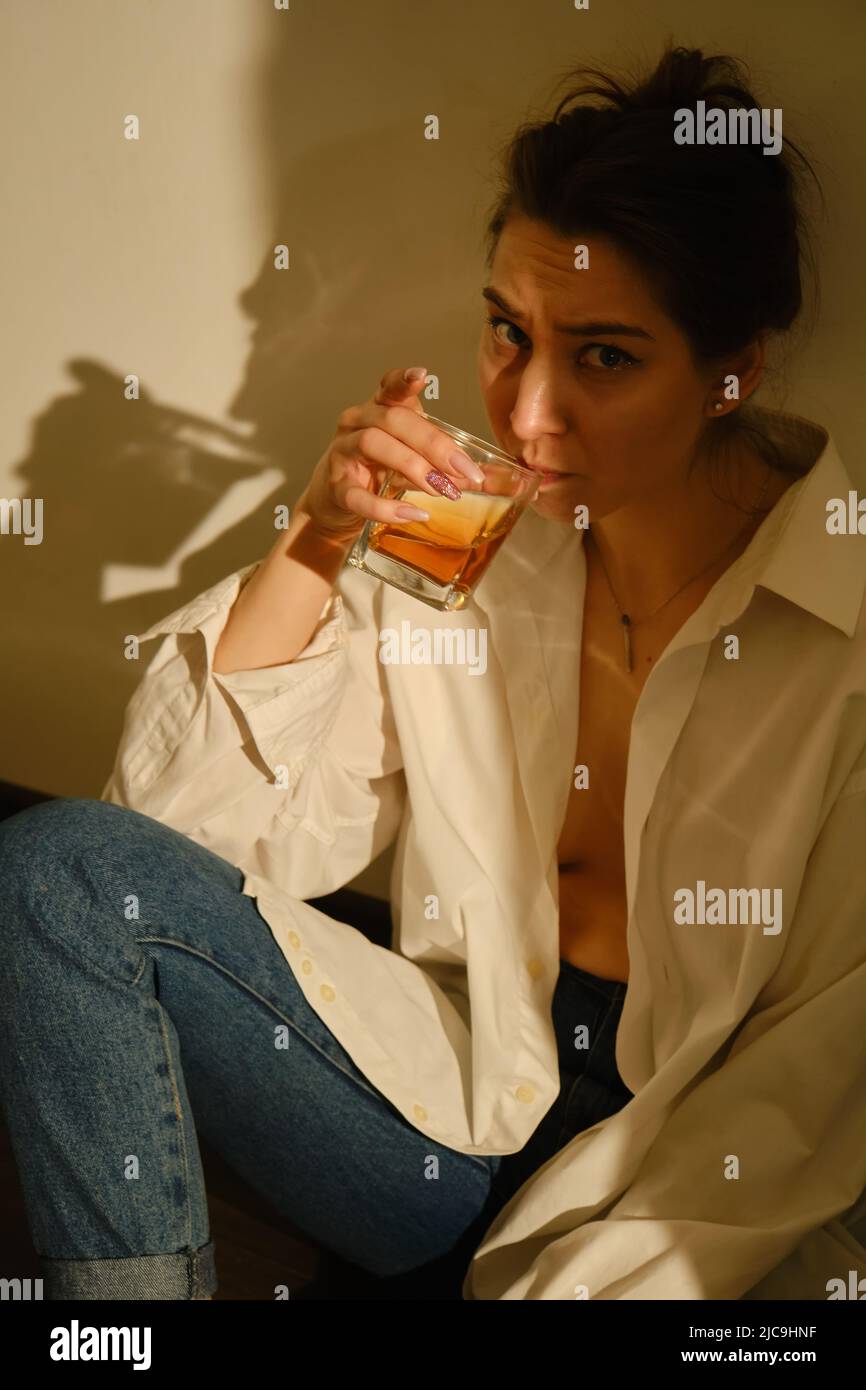 Young woman drinking alcohol from glass against sunny wall background ...