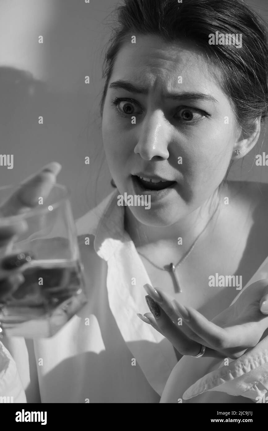 Young woman drinking alcohol from glass against sunny wall background ...