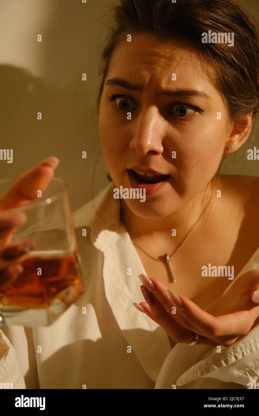 Young woman drinking alcohol from glass against sunny wall background ...