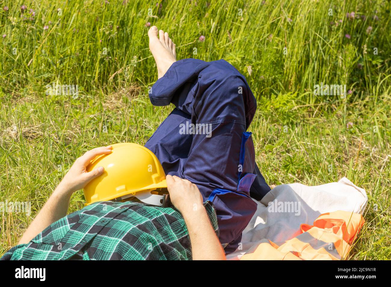 Worker relaxes lying on a meadow with a helmet and in working clothes ...