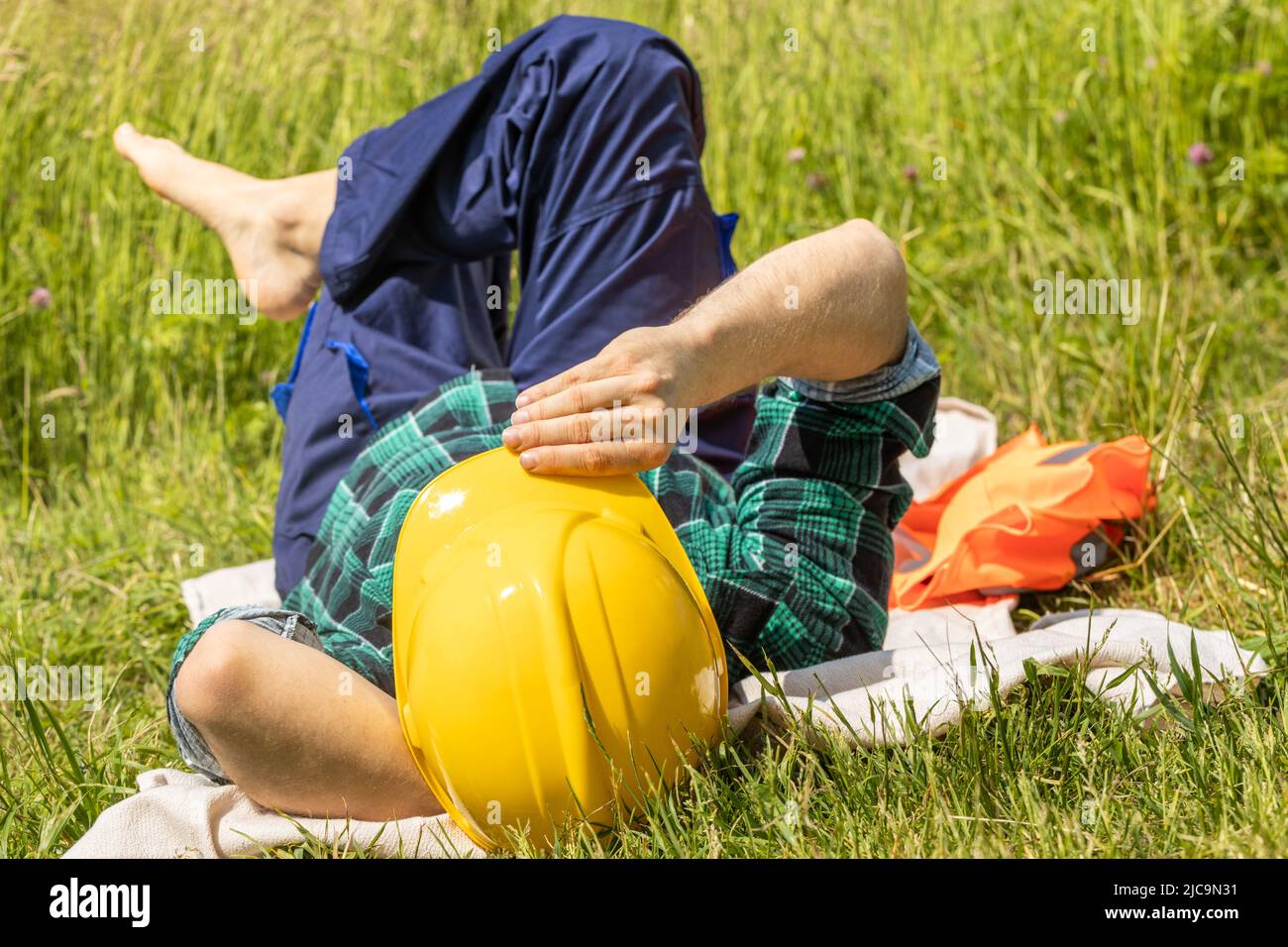 Worker relaxes lying on a meadow with a helmet and in working clothes ...