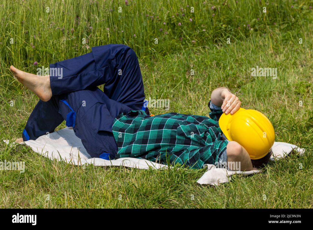 Worker relaxes lying on a meadow with a helmet and in working clothes ...