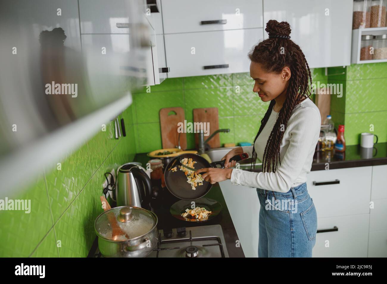Happy pretty mixed-race female cooking in kitchen in apartment serving ...