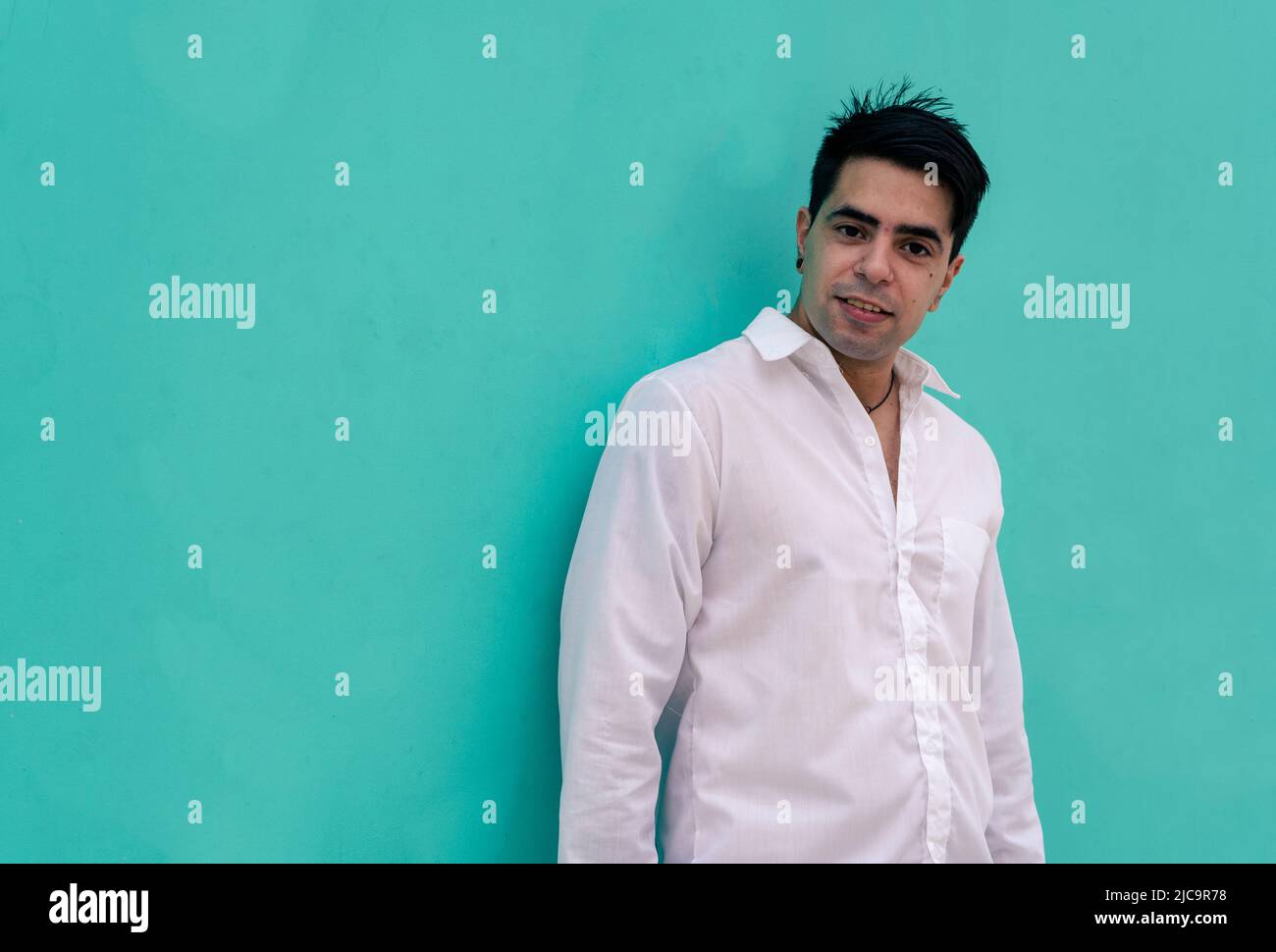 Half-length photograph of a young Latino guy leaning against a plain ...