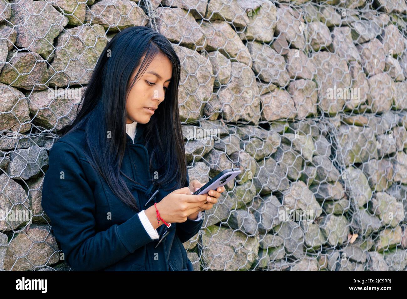 Young Latin woman in a black jacket checking and sending text messages ...