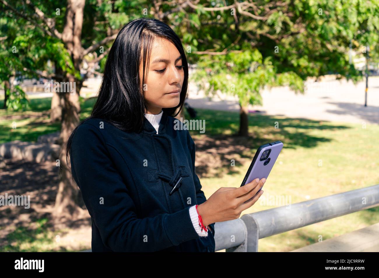 Young Latina woman checking and texting from her smartphone leaning ...