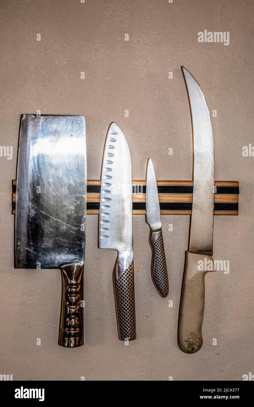 Four well-used chefs knives on a magnetic holder mounted on textured ...