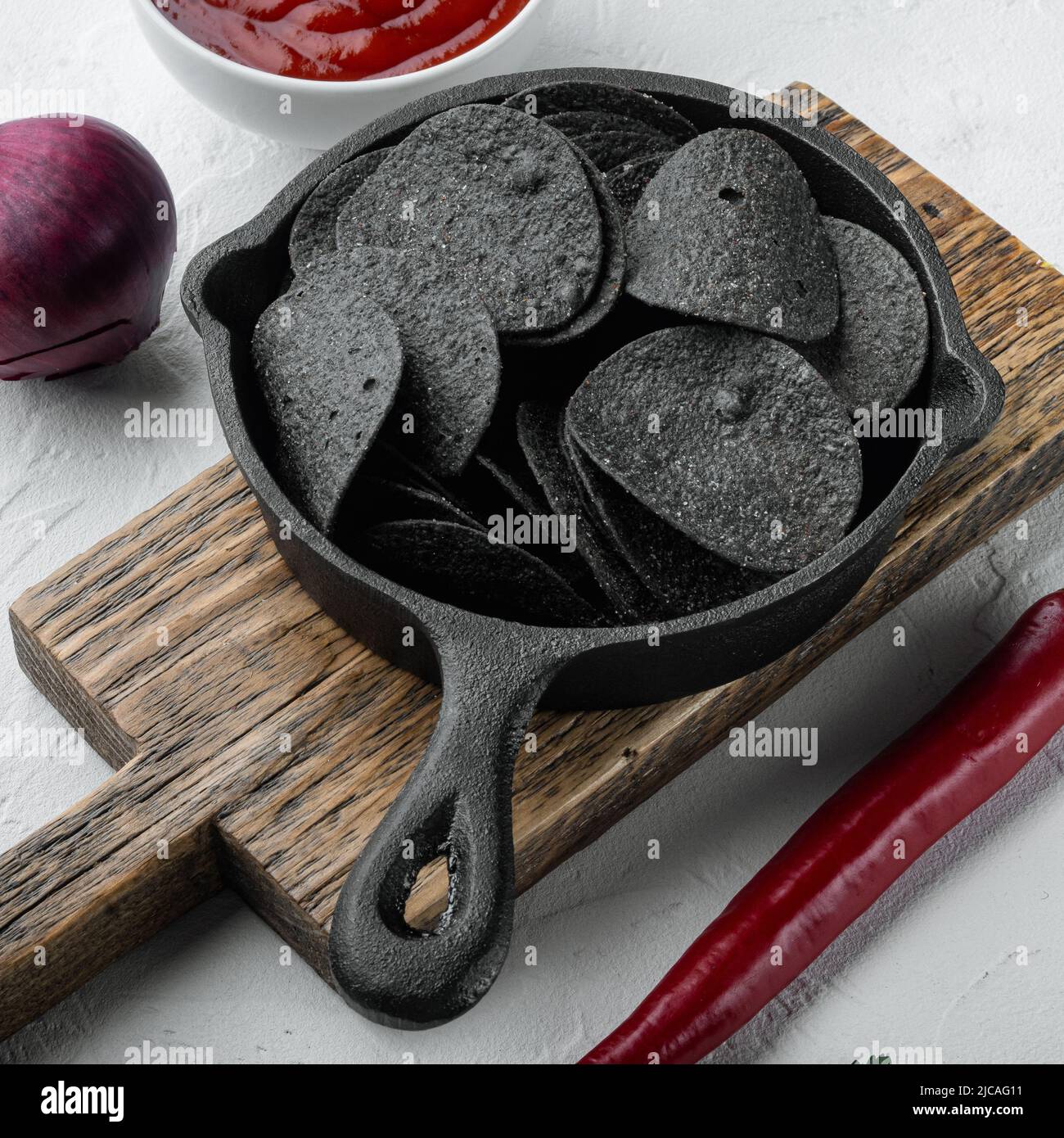 Black crispy potato chips, in cast iron frying pan, on white stone ...