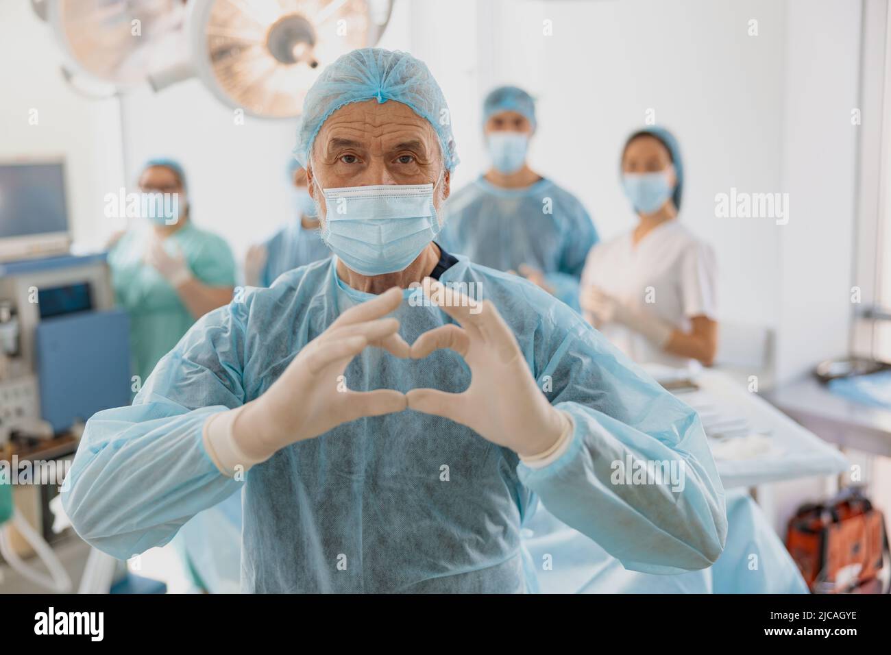 Senior surgeon in protective medical mask shows heart with his hands ...