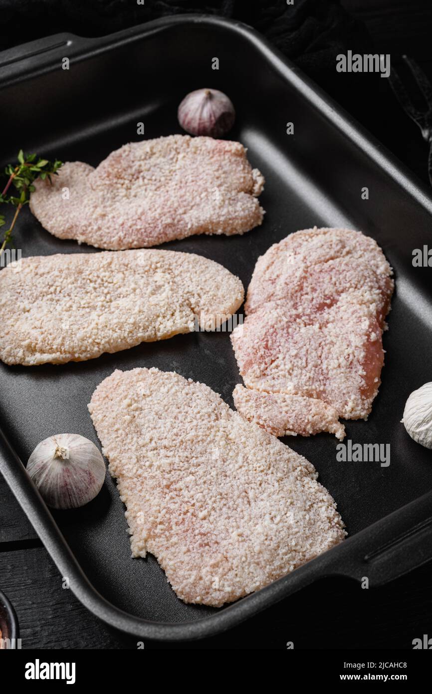 Homemade raw breaded German Weiner Schnitzel set, on black wooden table ...