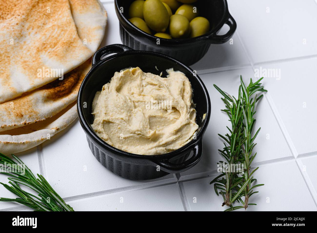 Bowl of tasty fresh hummus set, on white ceramic squared tile table ...