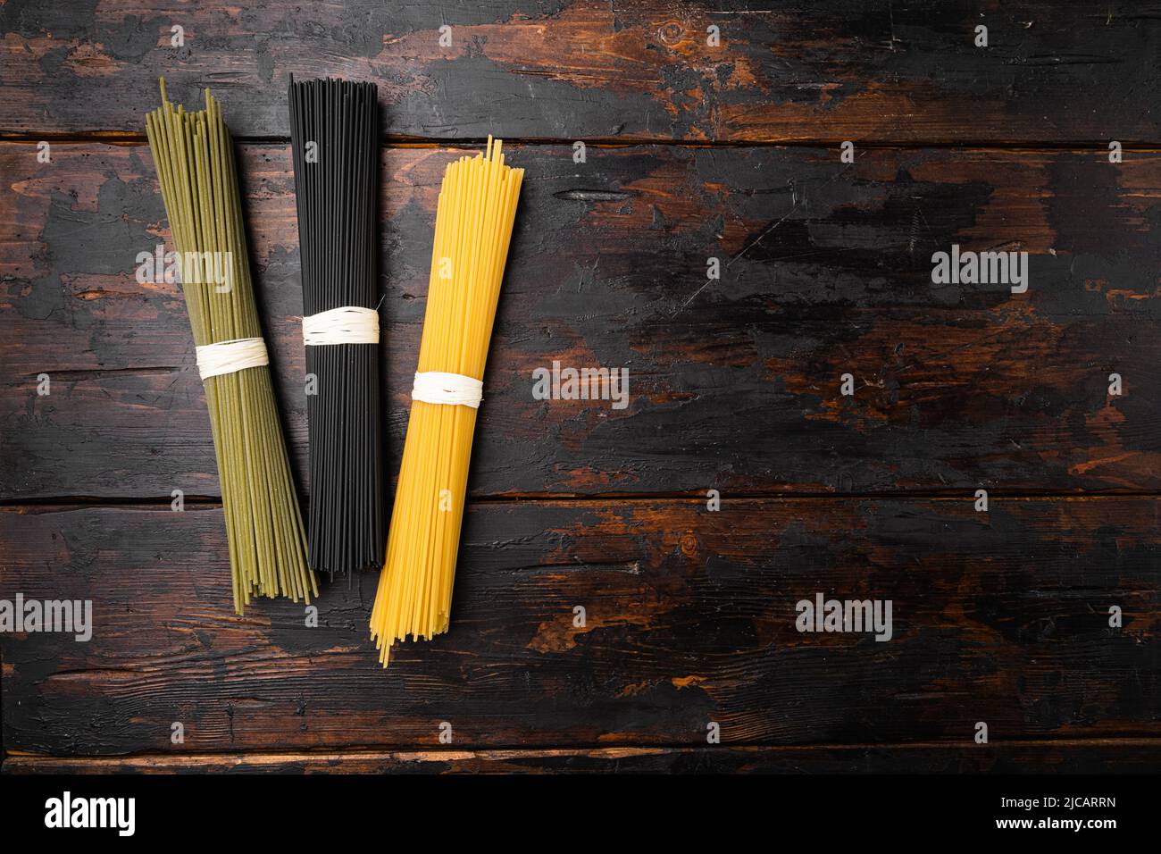 Multi colored spaghetti with ingredients, on old dark wooden table ...