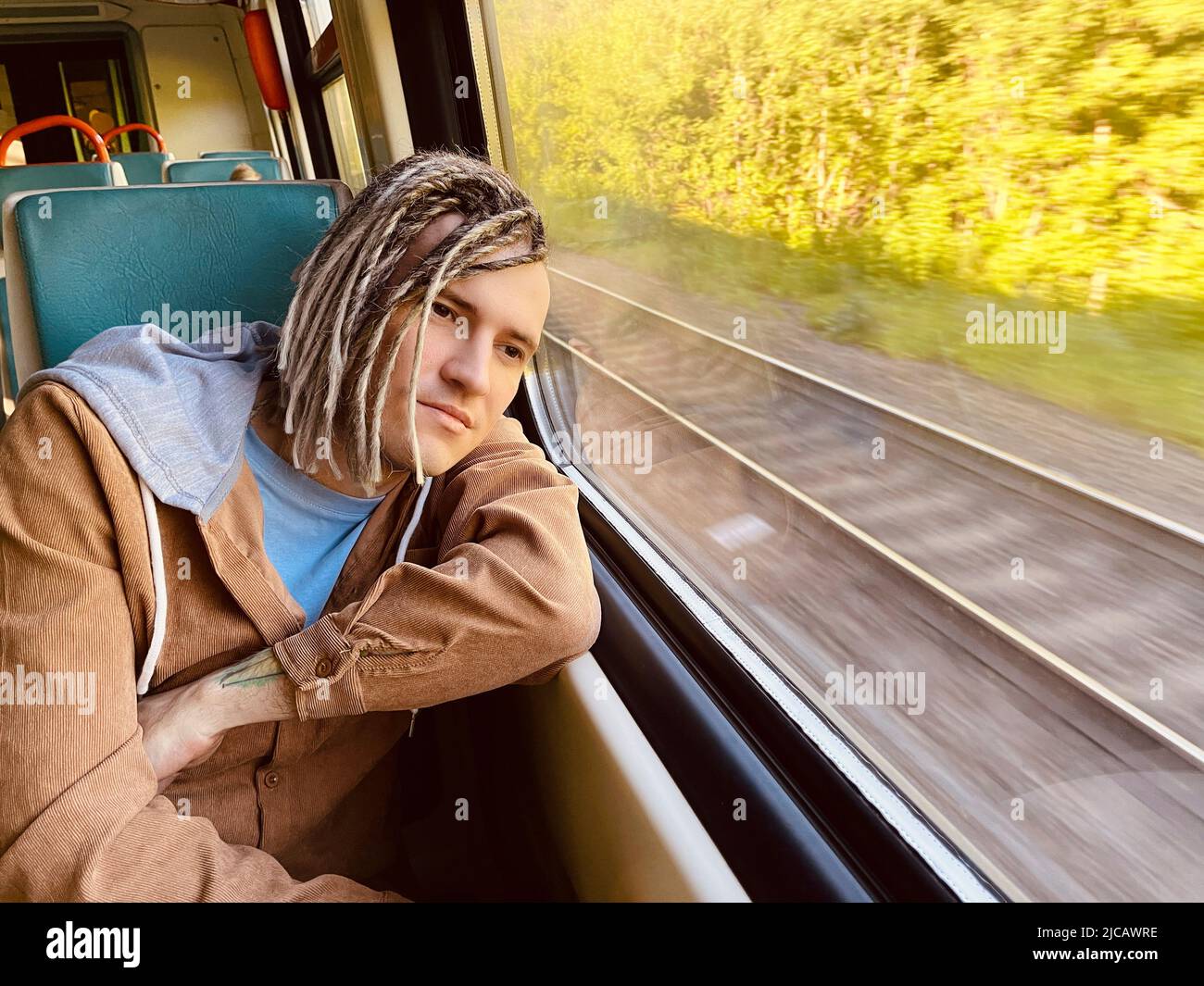 Young relaxed man riding on train. Dreamy guy with blonde dreadlocks ...
