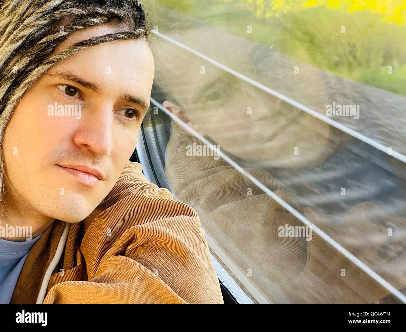 Young relaxed man riding on train. Dreamy guy with blonde dreadlocks ...