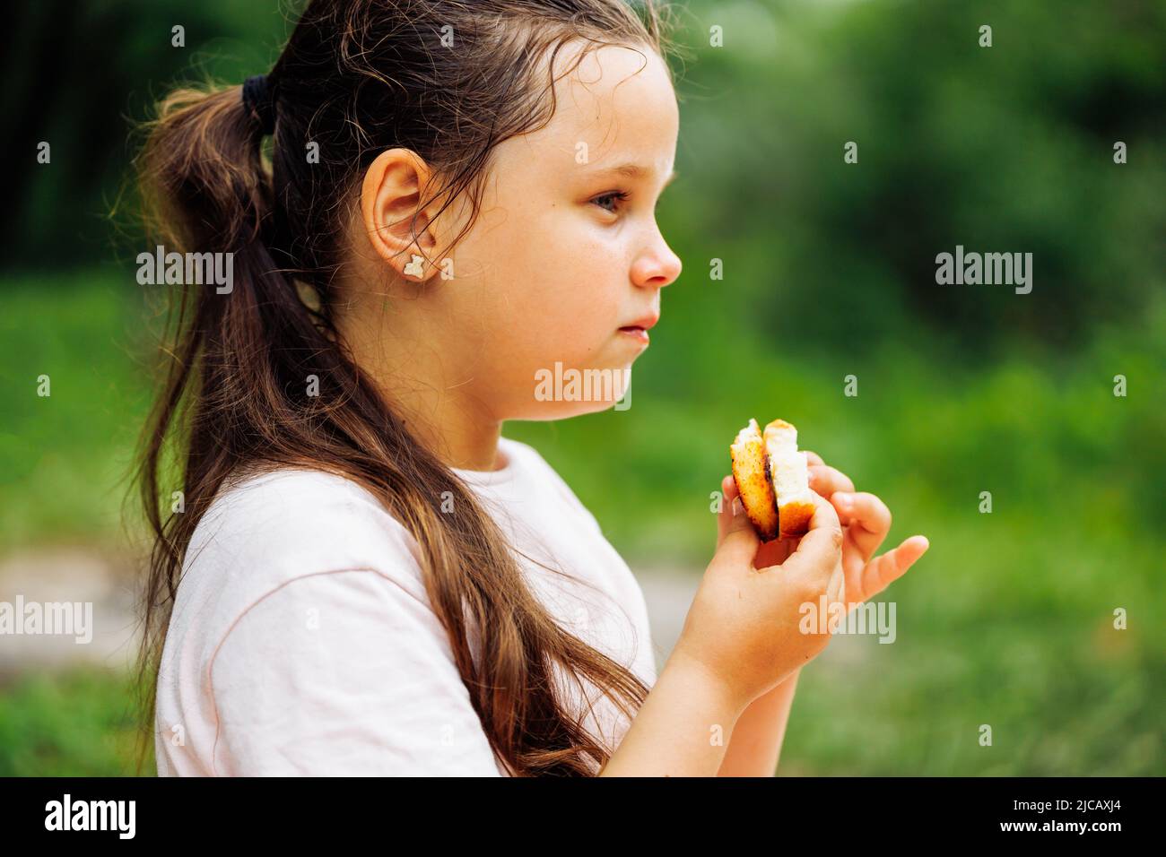 Side view of little thoughtful girl wth dark hair holding sandwich ...