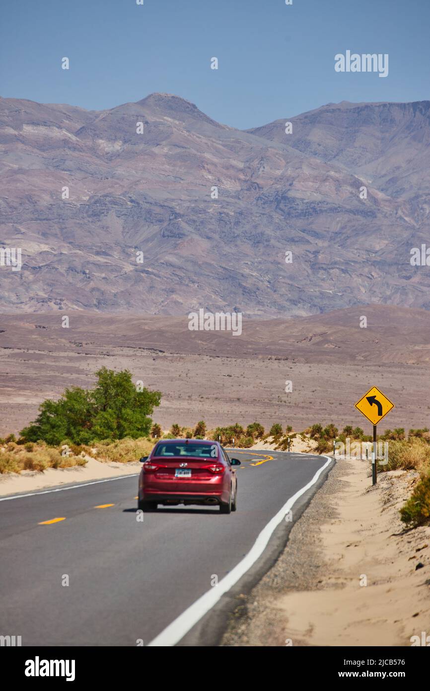 Red car driving down desert road leading to sharp turn and mountains ...
