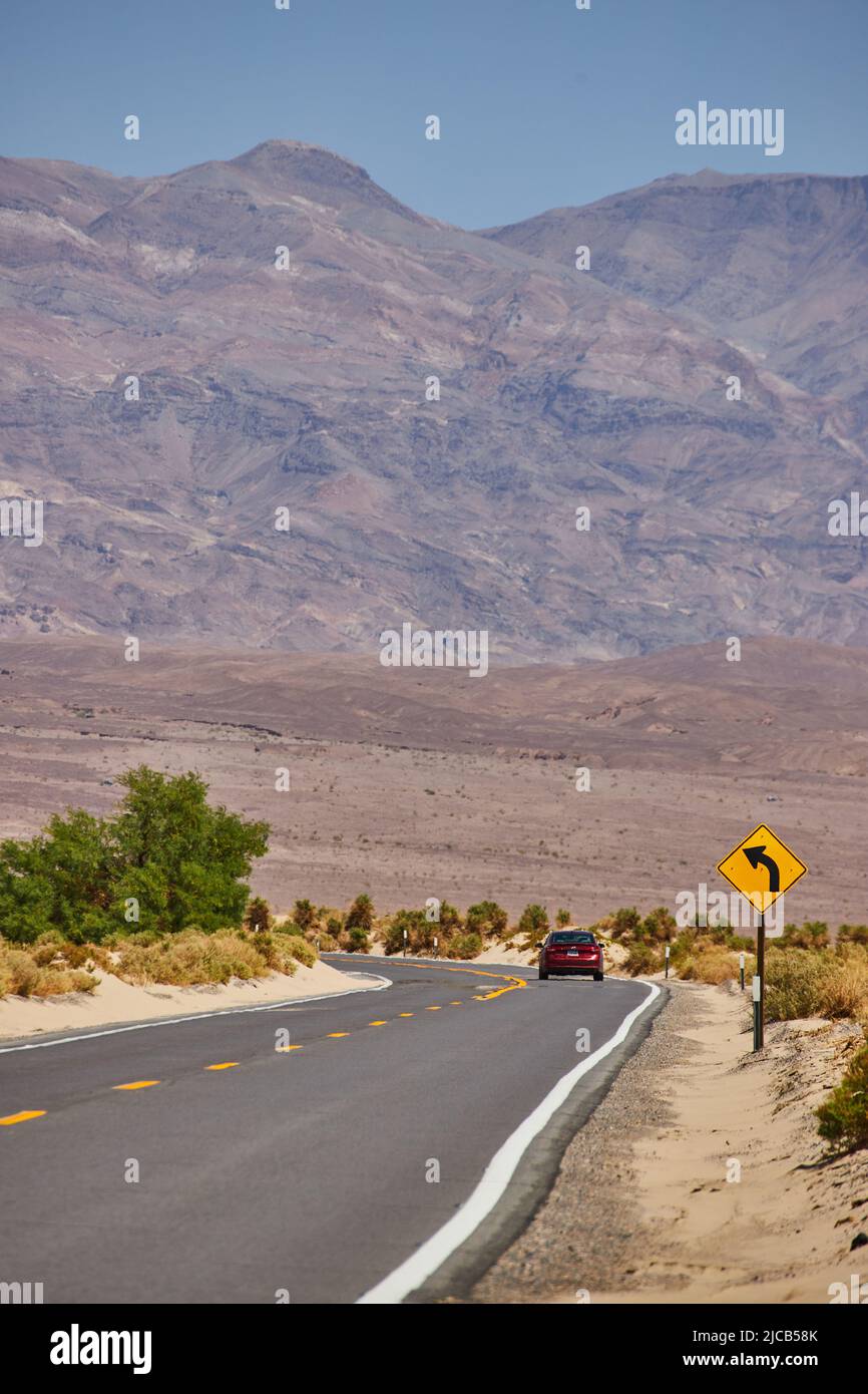 Red car making sharp turn on paved road in desert leading to mountains ...