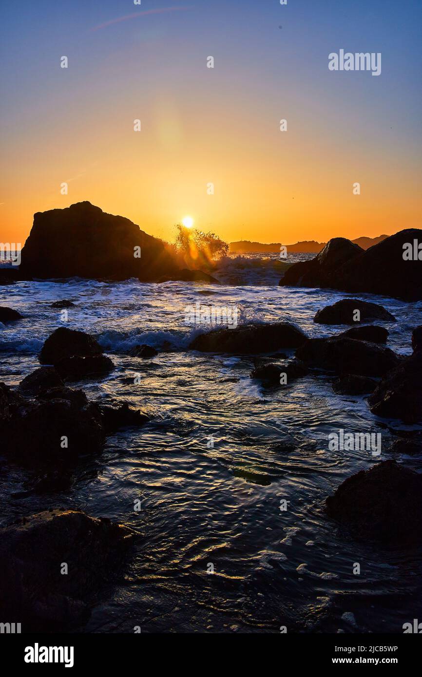 Sun sets on beach with waves and rocks Stock Photo - Alamy