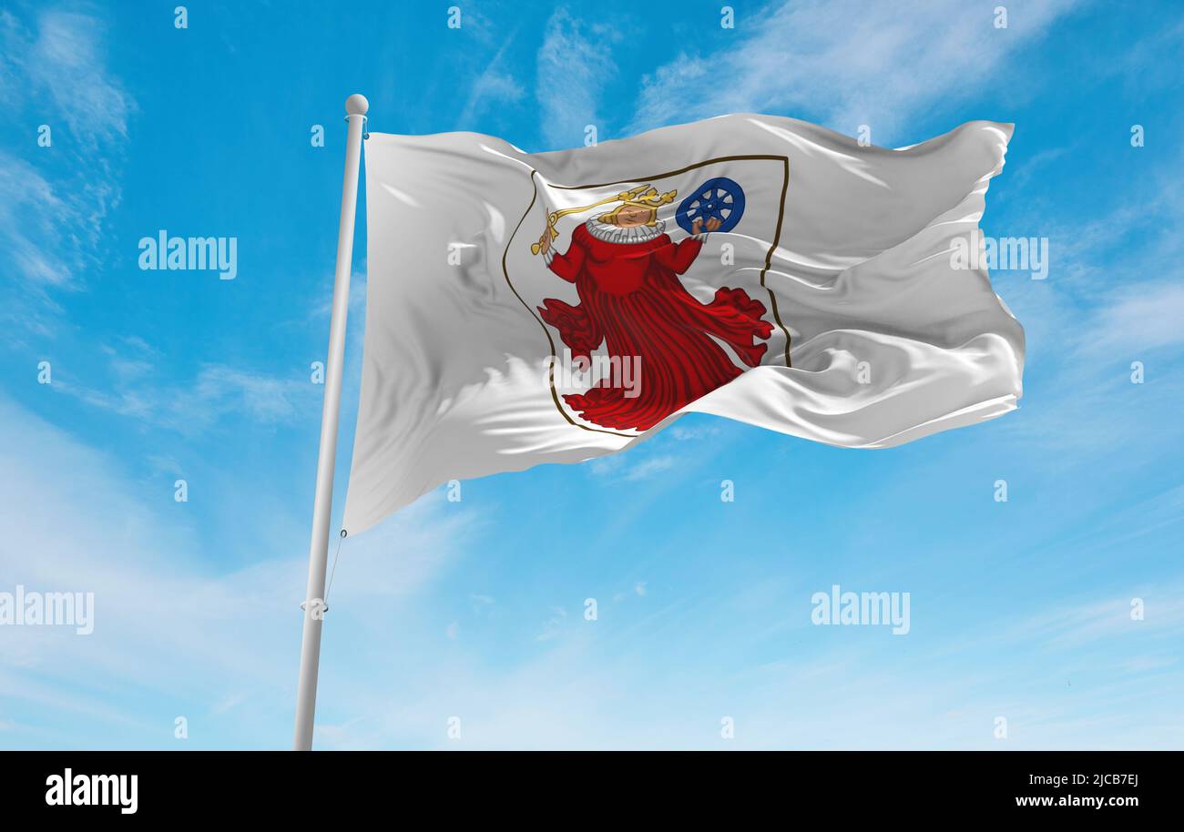 official flag of Hjorring , Denmark at cloudy sky background on sunset ...