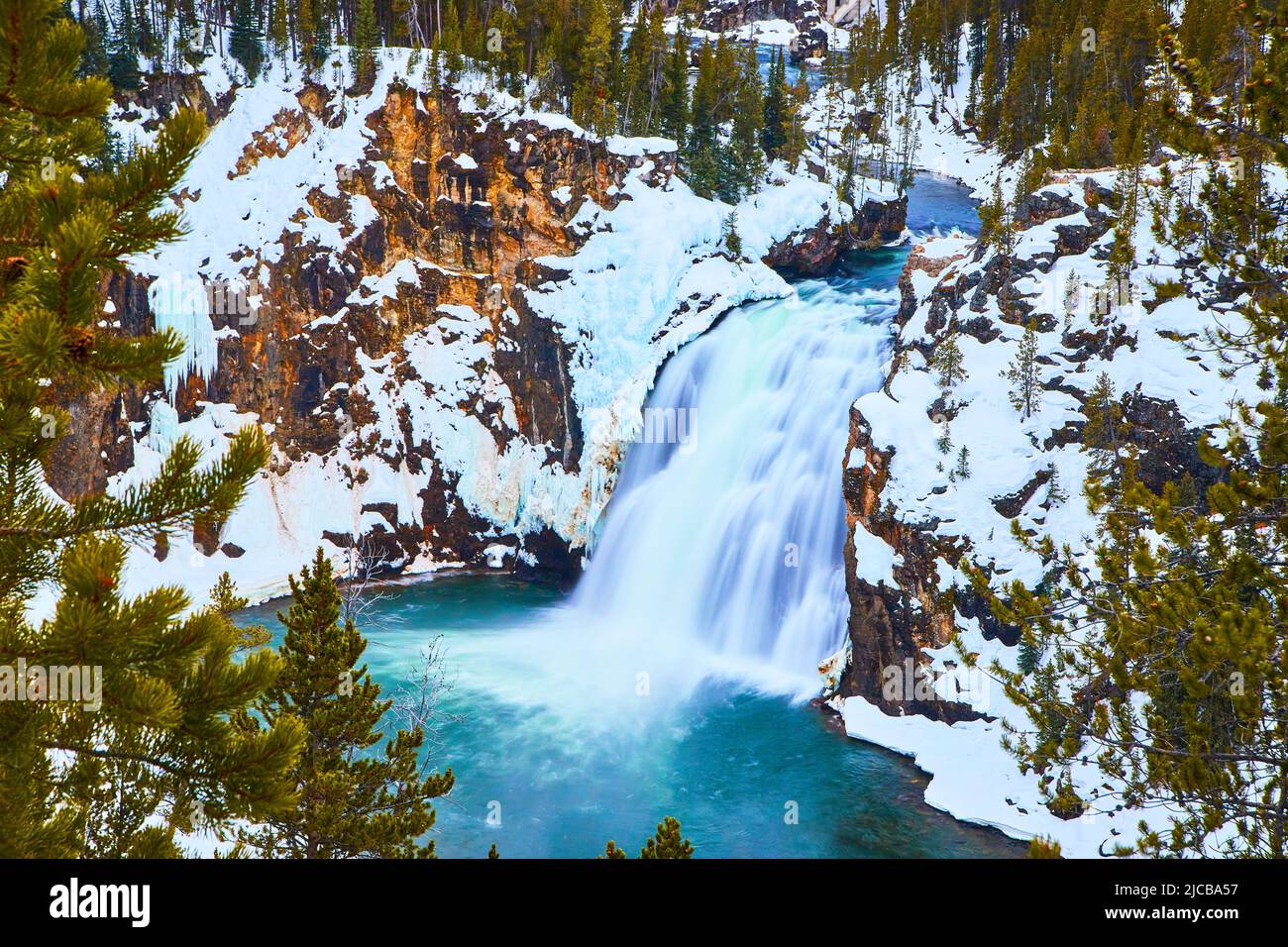 Pine trees frame snowy cliffs and stunning blue waterfalls in ...