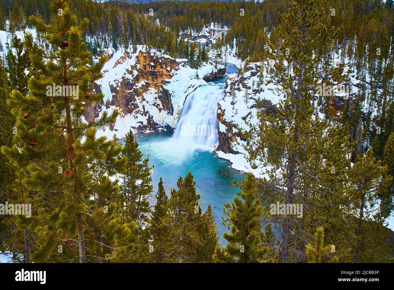 Pine trees frame serene blue waterfalls in winter at Yellowstone Stock ...