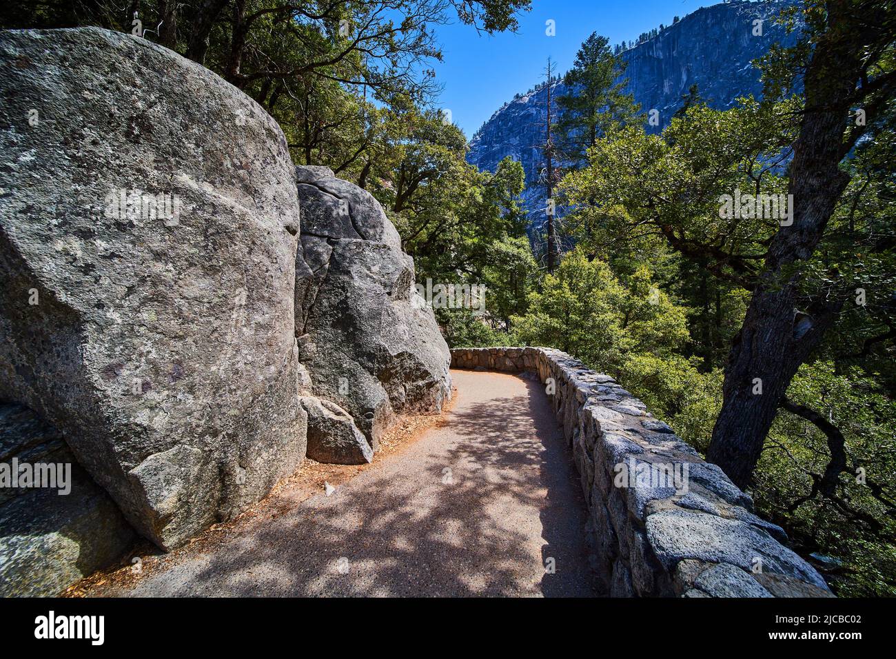 Paved hiking path alongside large boulders with stone wall Stock Photo ...