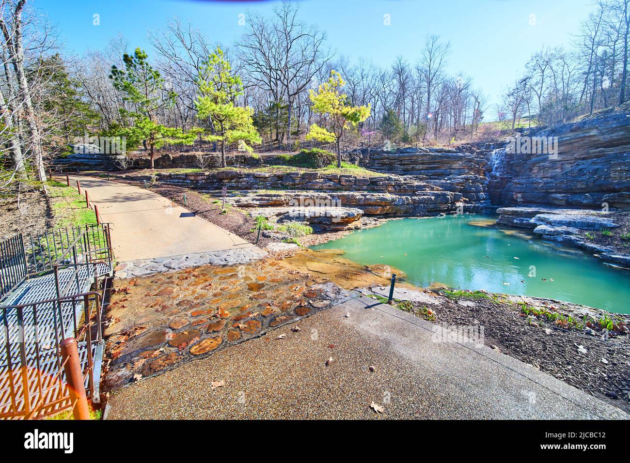 Paved walking path next to teal waters with cliffs and waterfall Stock ...