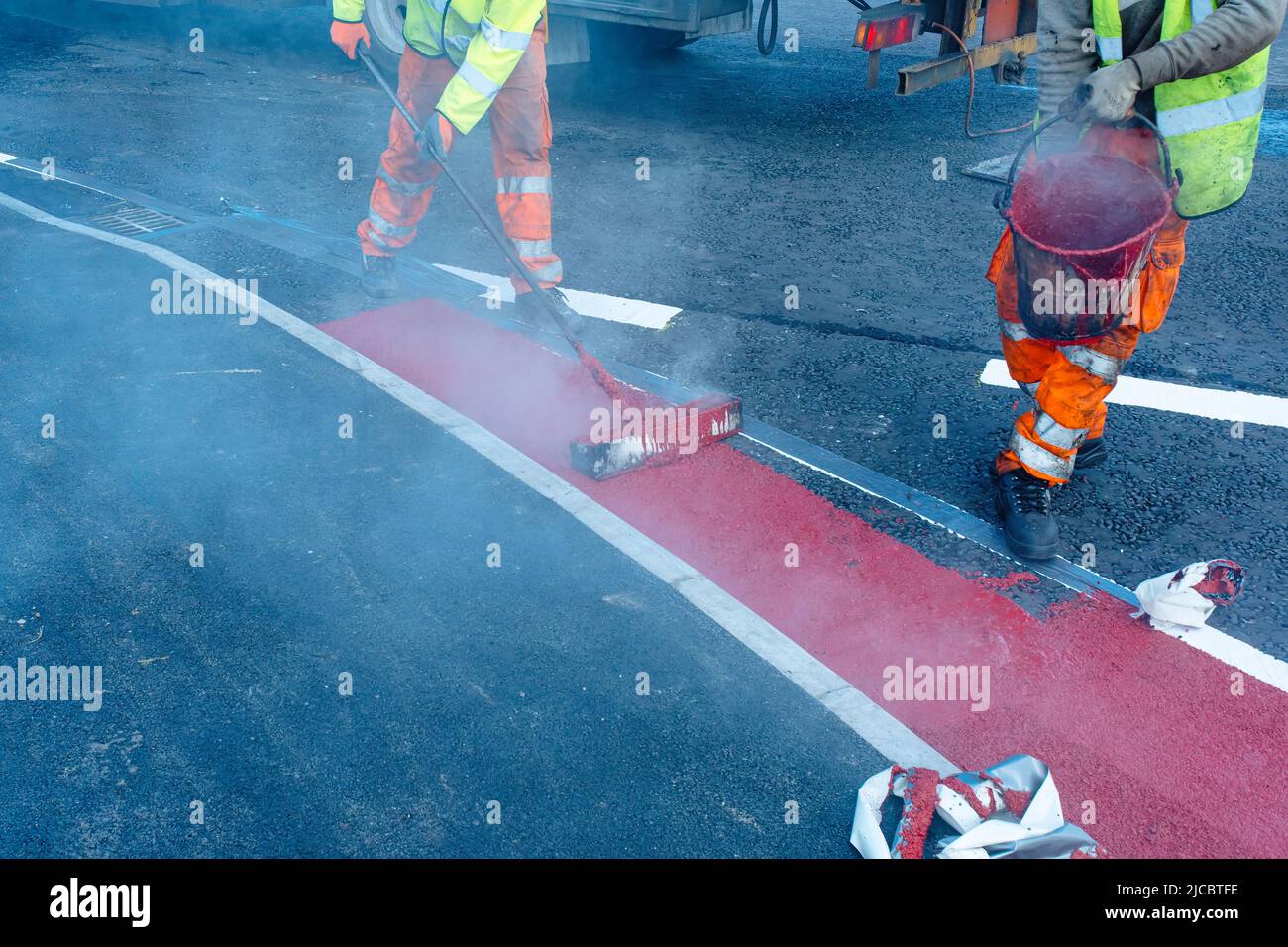 Road workers applying hot red road marking paint on new build road ...