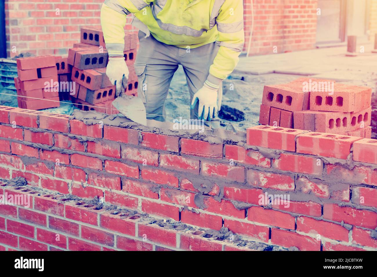 Bricklayer in safety vest and a helmet laying a brick wall using a ...