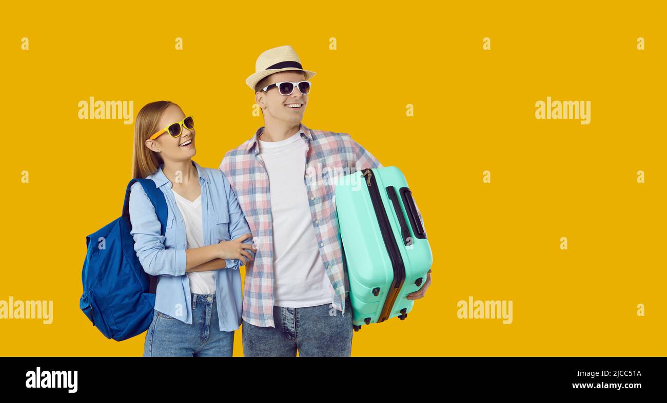 Happy couple who are going on holiday trip standing isolated on yellow ...