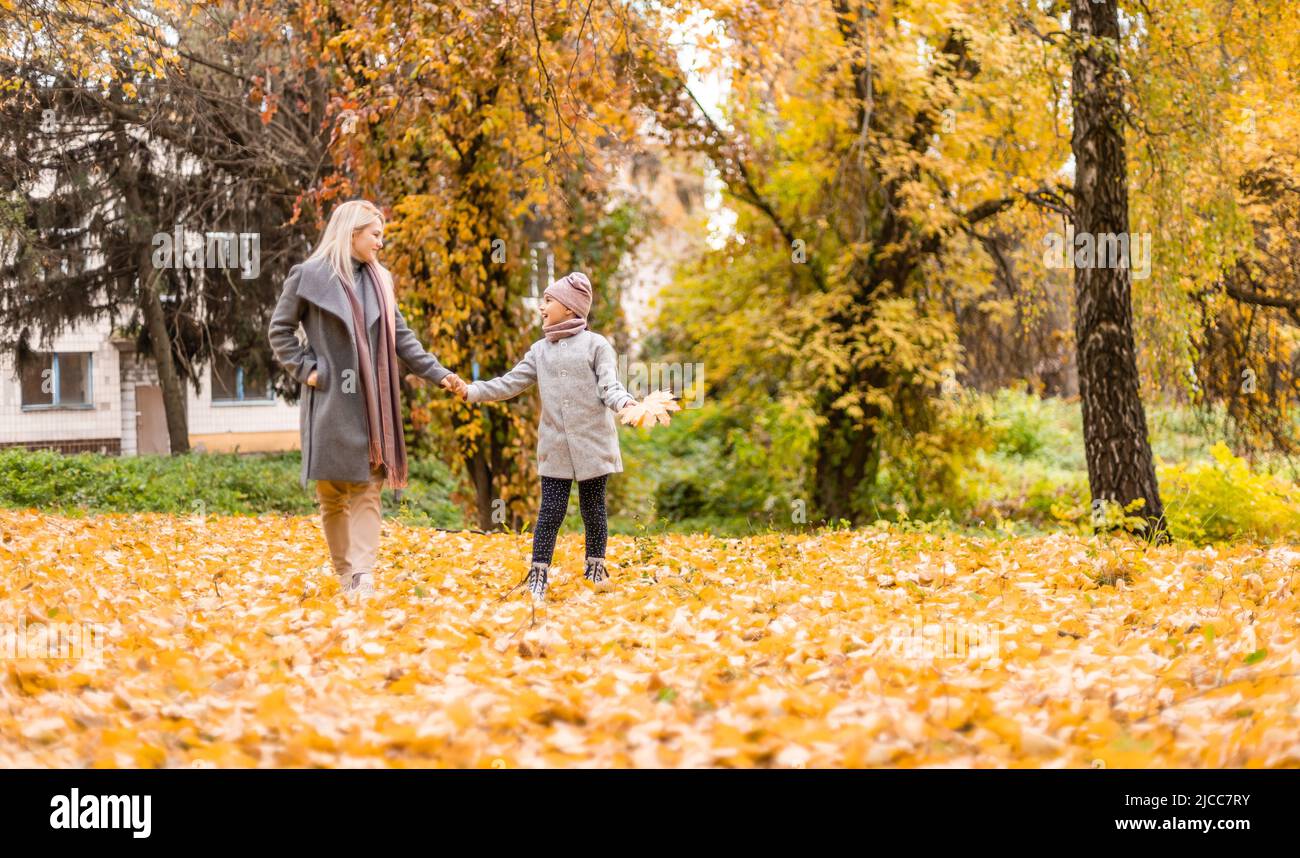 Mother and daughter having fun in the autumn park among the falling ...