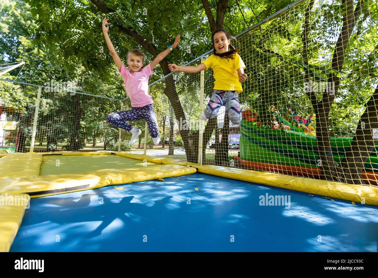 Two little girls in the summer jump on a trampoline, smiling and ...
