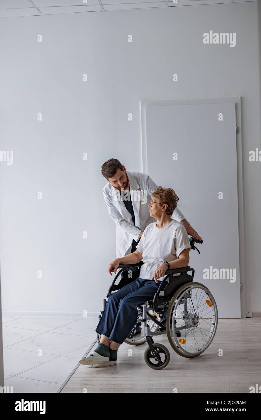 Professional male doctor carrying female patient on wheelchair in ...